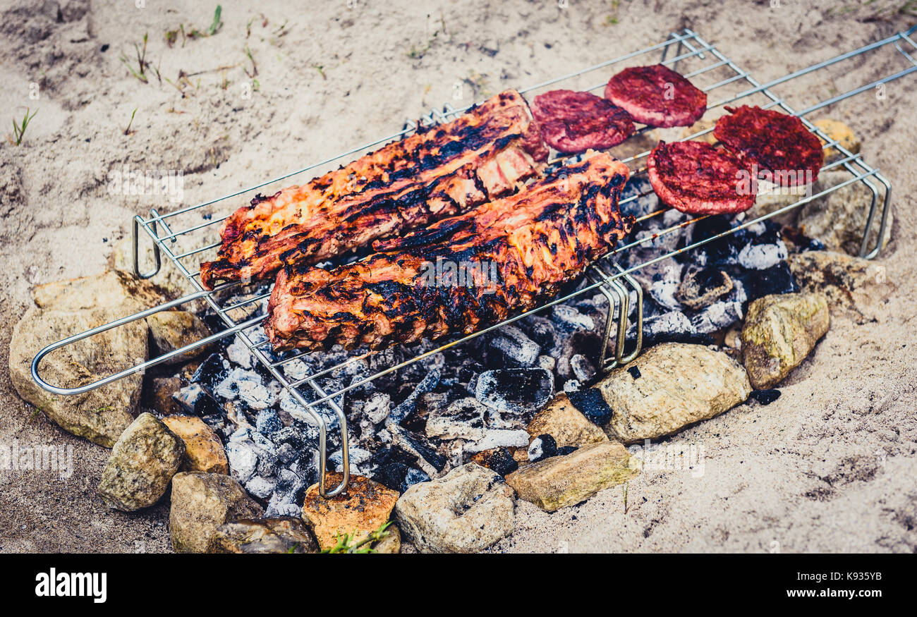 Pork ribs and burgers on homemade improvised BBQ barbecue grill. Making ...