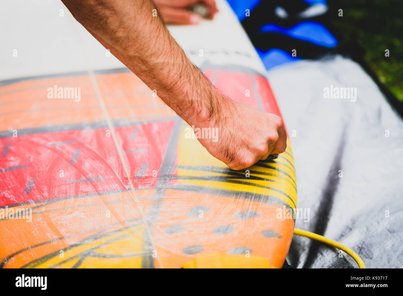 Close up view of hand waxing surf board outdoors. Man is removing or ...