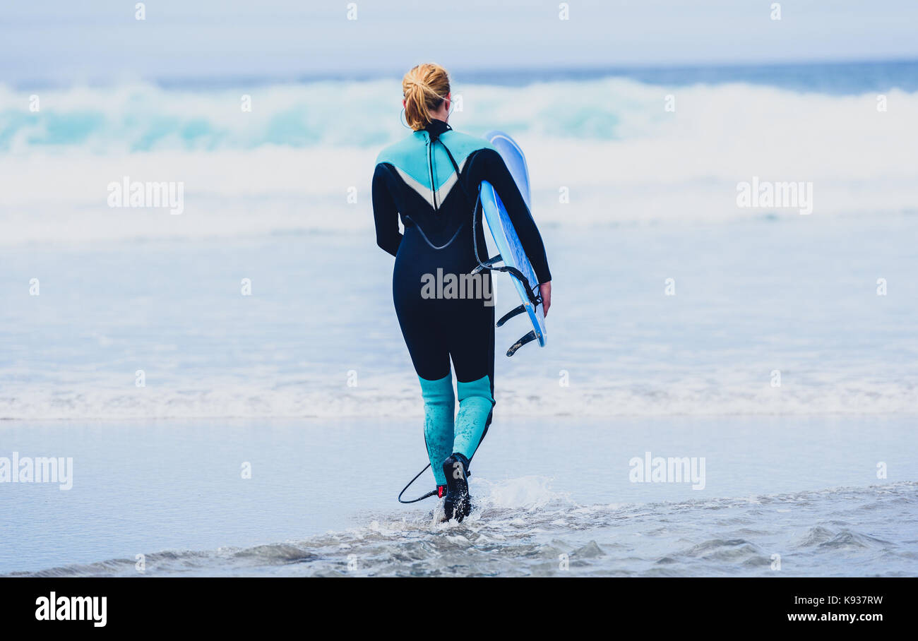 Surfer woman with surfboard is walking and watching the waves. Girl in ...