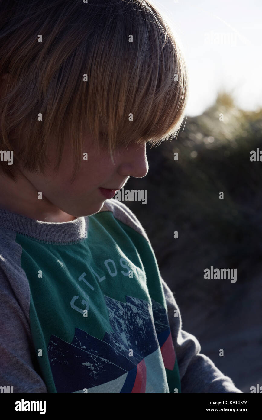 A young boy looking down at this hands on the sand dunes at sunset ...