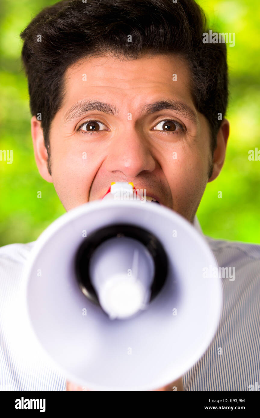 Portrait of a handsome man shouting with a megaphone in a blurred green ...