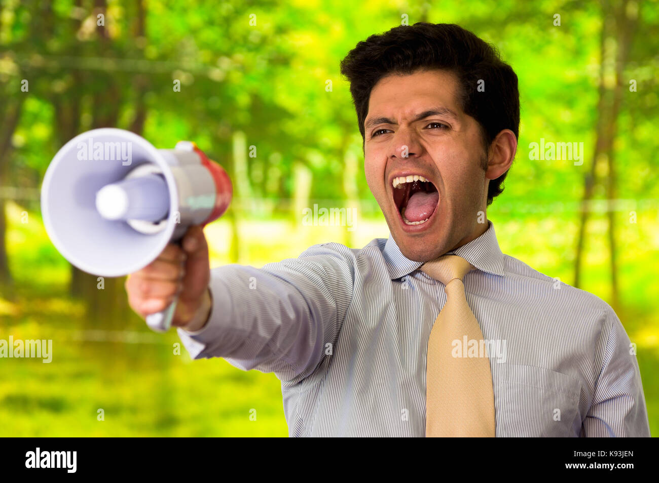 Portrait of a young man screaming with a megaphone, in a blurred green ...