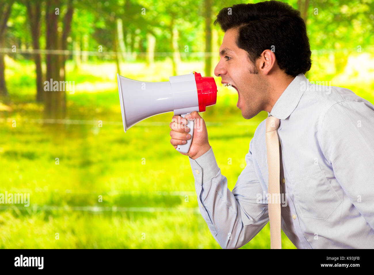 Portrait of a young man screaming with a megaphone, in a blurred green ...