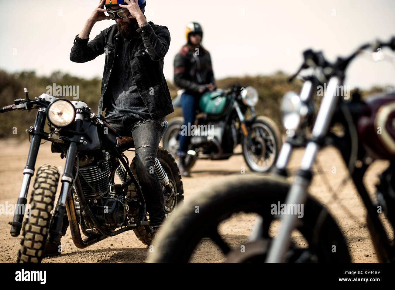 Three men sitting on cafe racer motorcycles on a dusty dirt road Stock ...