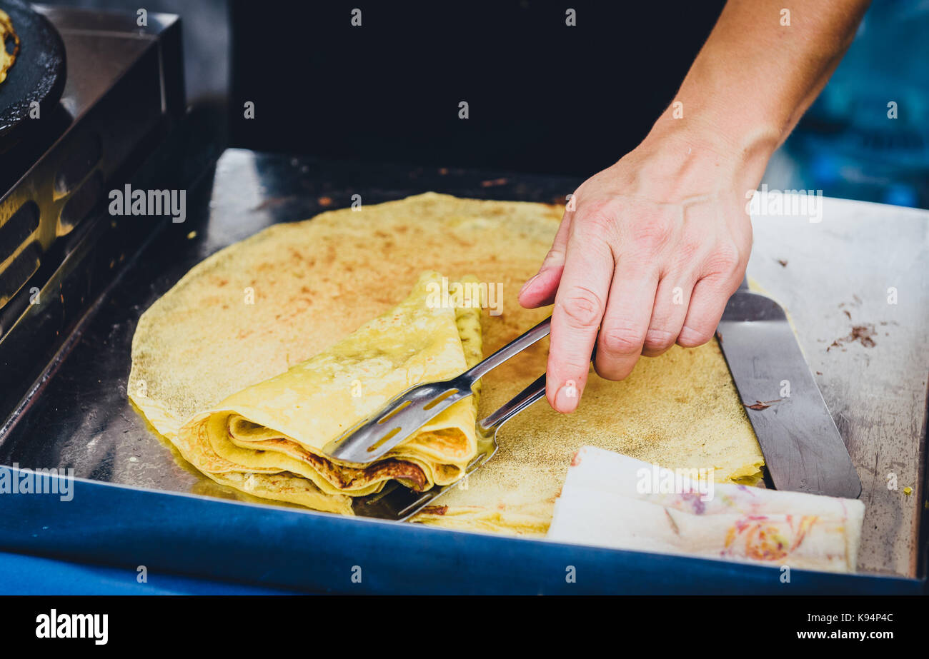 Making of crepes pancakes in open market festival fair. A hand is ...