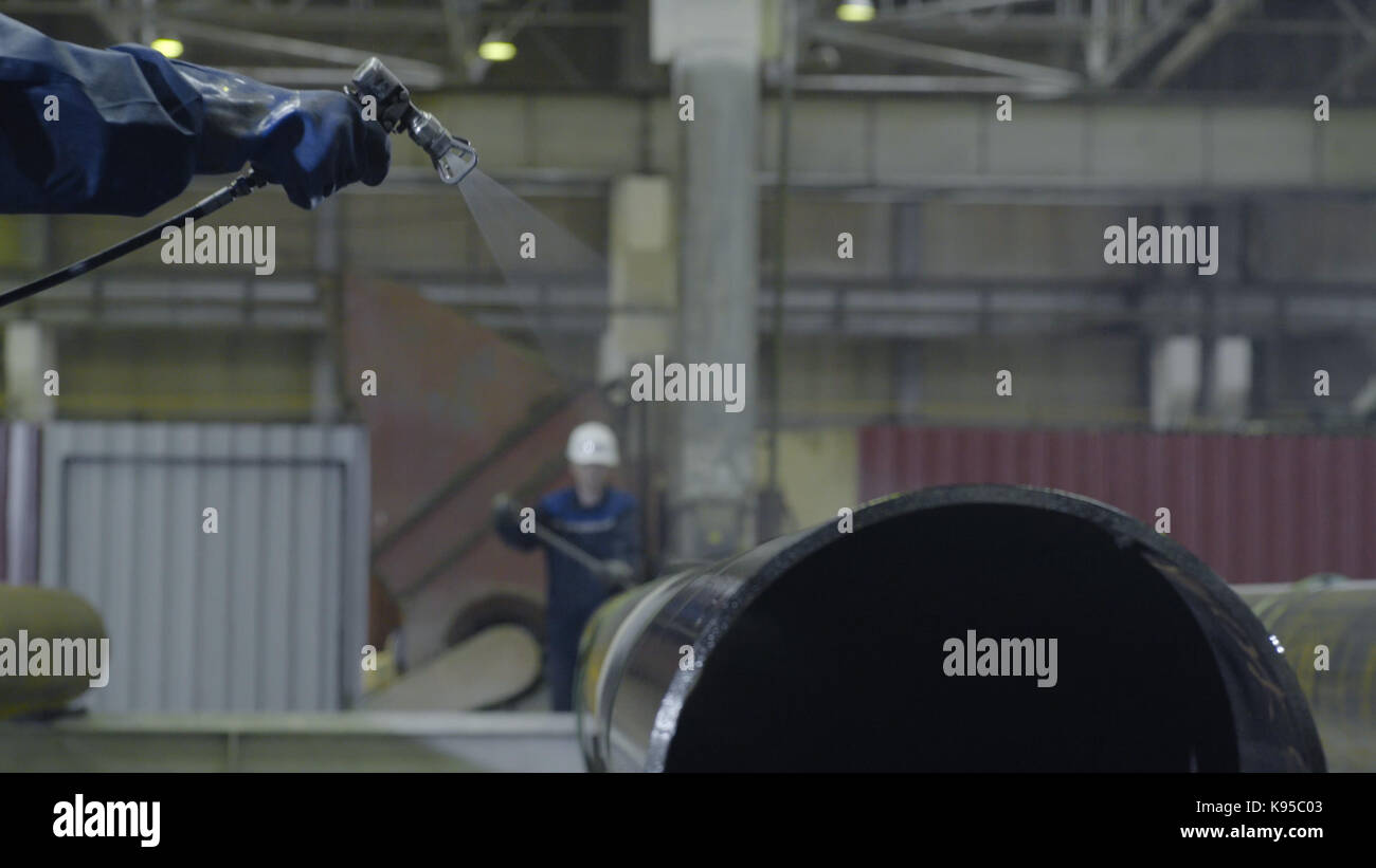 Man paints pipe atomizer. Mens hand paint the pipes on the plant ...