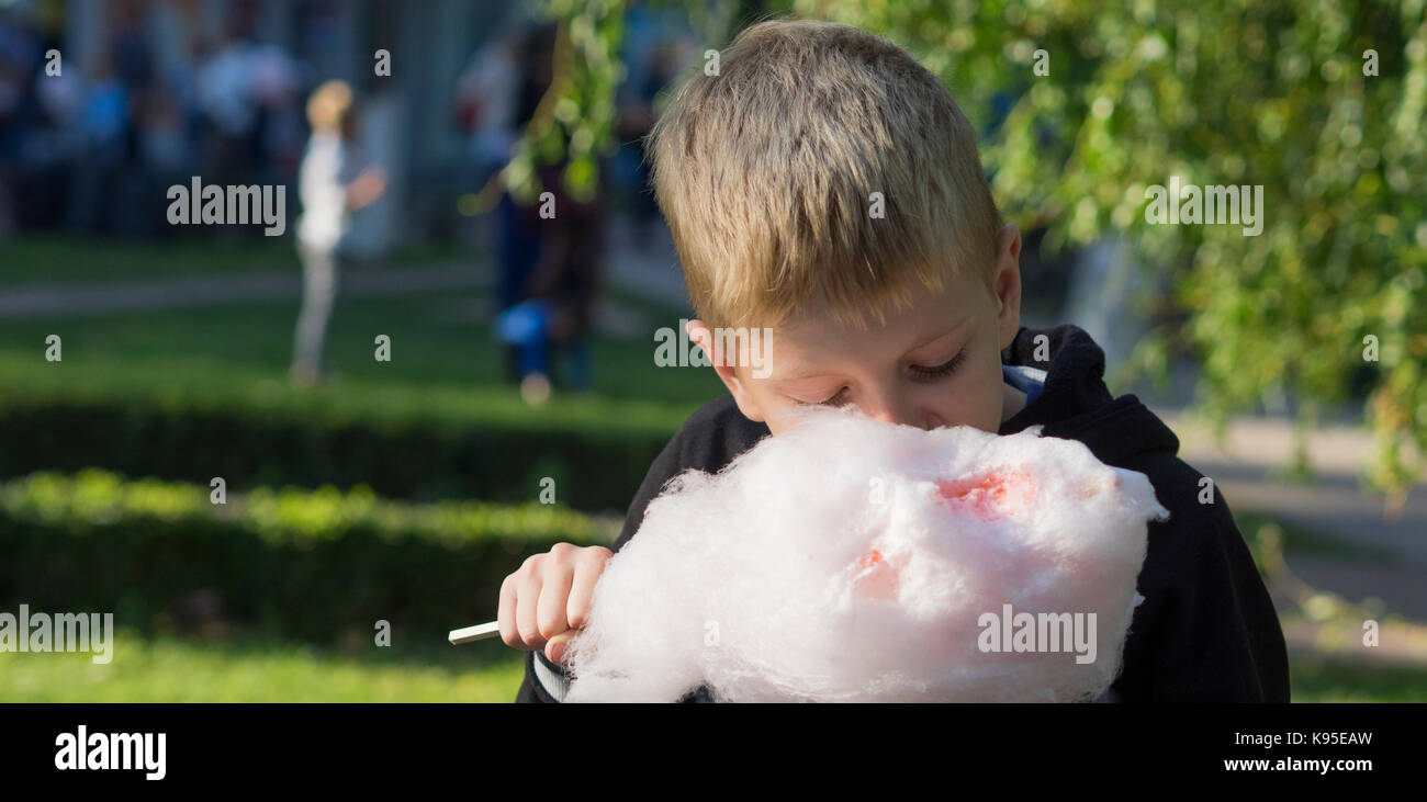boy eating a stick of candy floss or cotton candy made from sticky spun ...