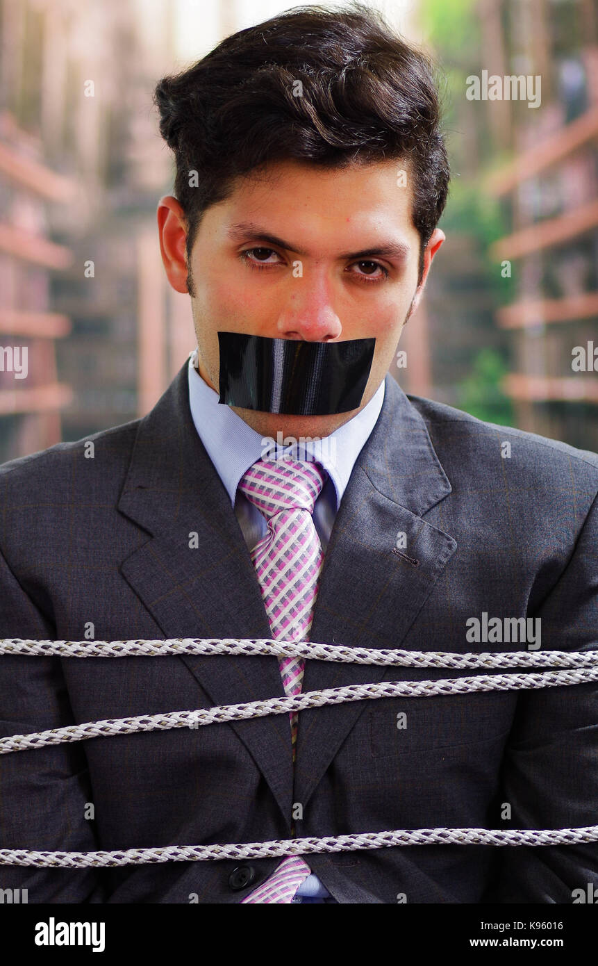 Businessman trapped in a chair with rope, with a black tape in his ...