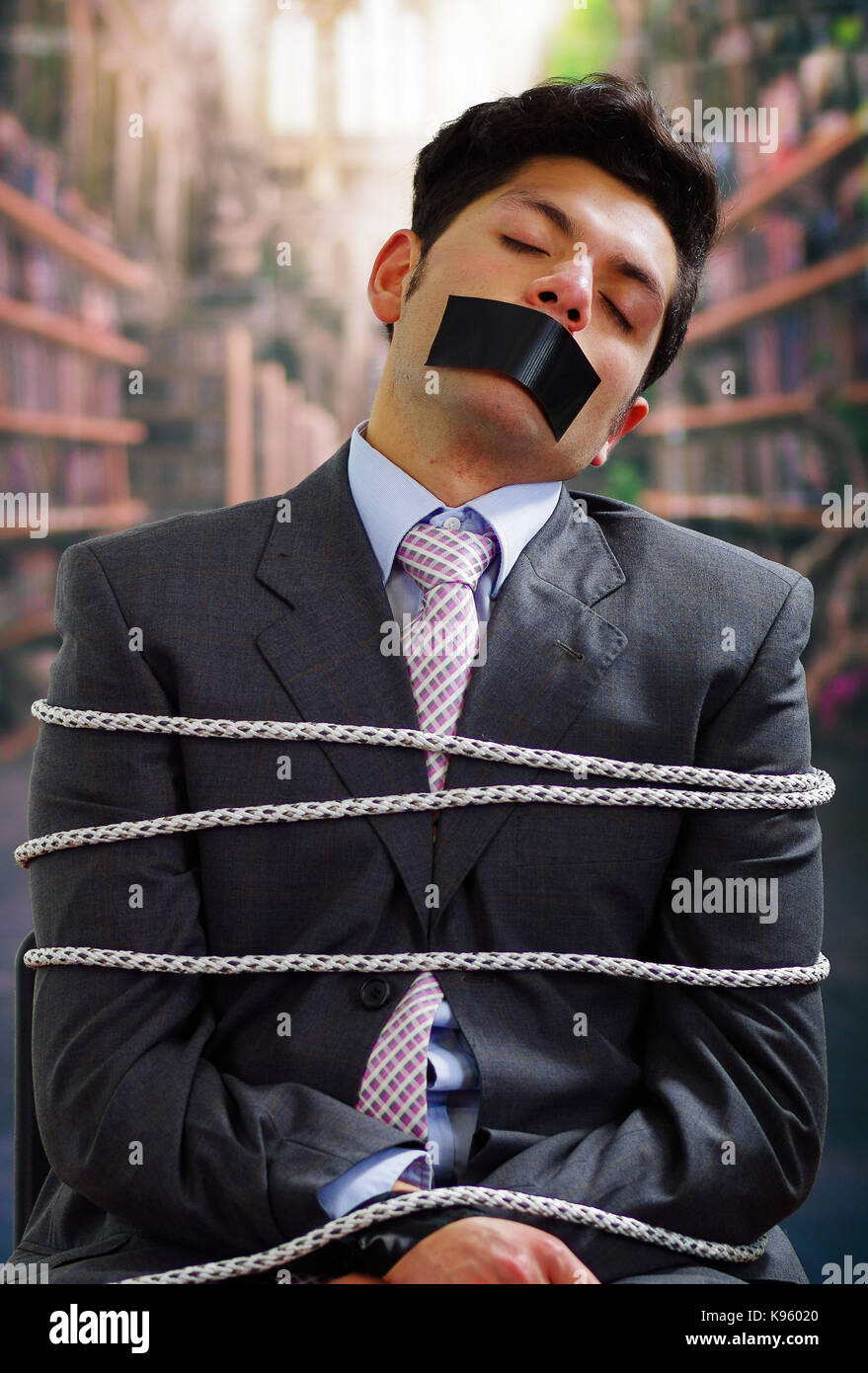 Businessman trapped in a chair with rope, with a black tape in his ...