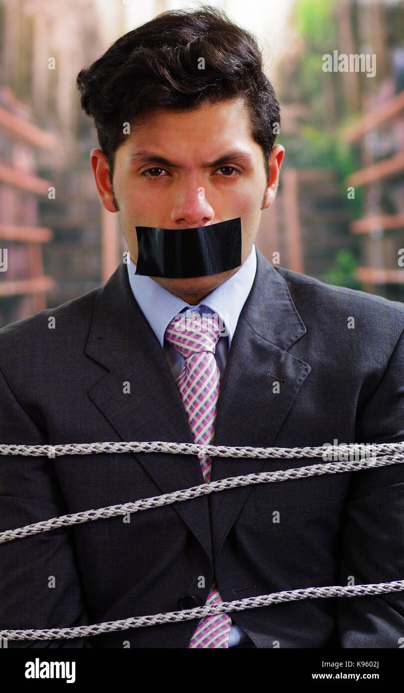 Businessman trapped in a chair with rope, with a black tape in his ...