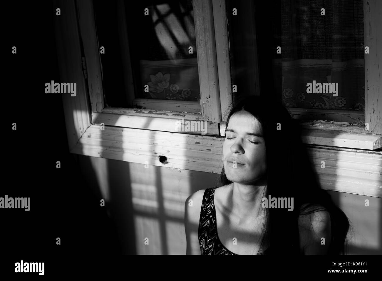 Young woman basking in the rays of the sun in the shadow of the window ...
