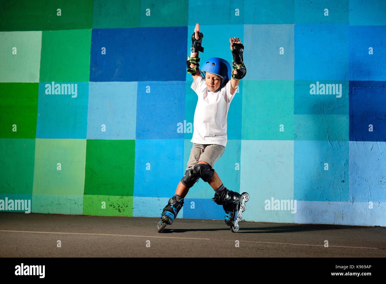 Cute little boy on roller skates running against the blue graffiti wall ...
