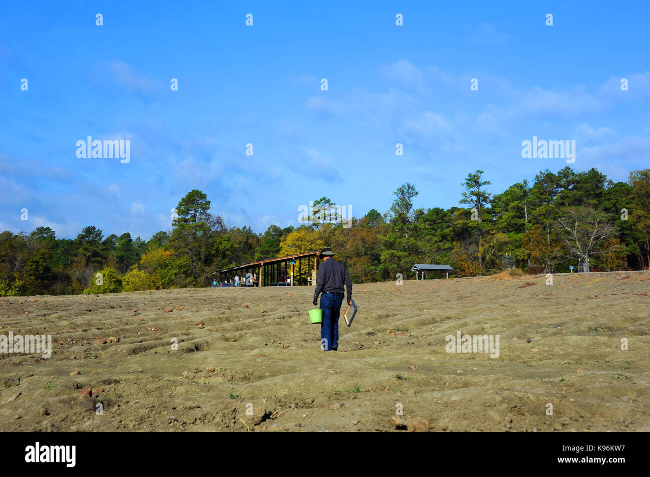 Man walks across diamond field as he carries his pail and screen to the ...