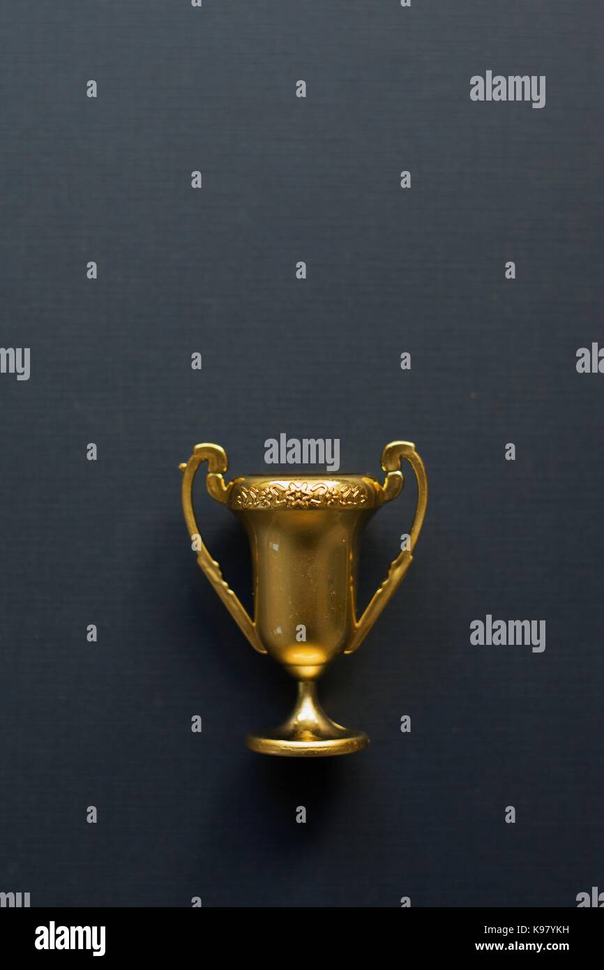 A gold trophy against a plain dark blue background Stock Photo - Alamy