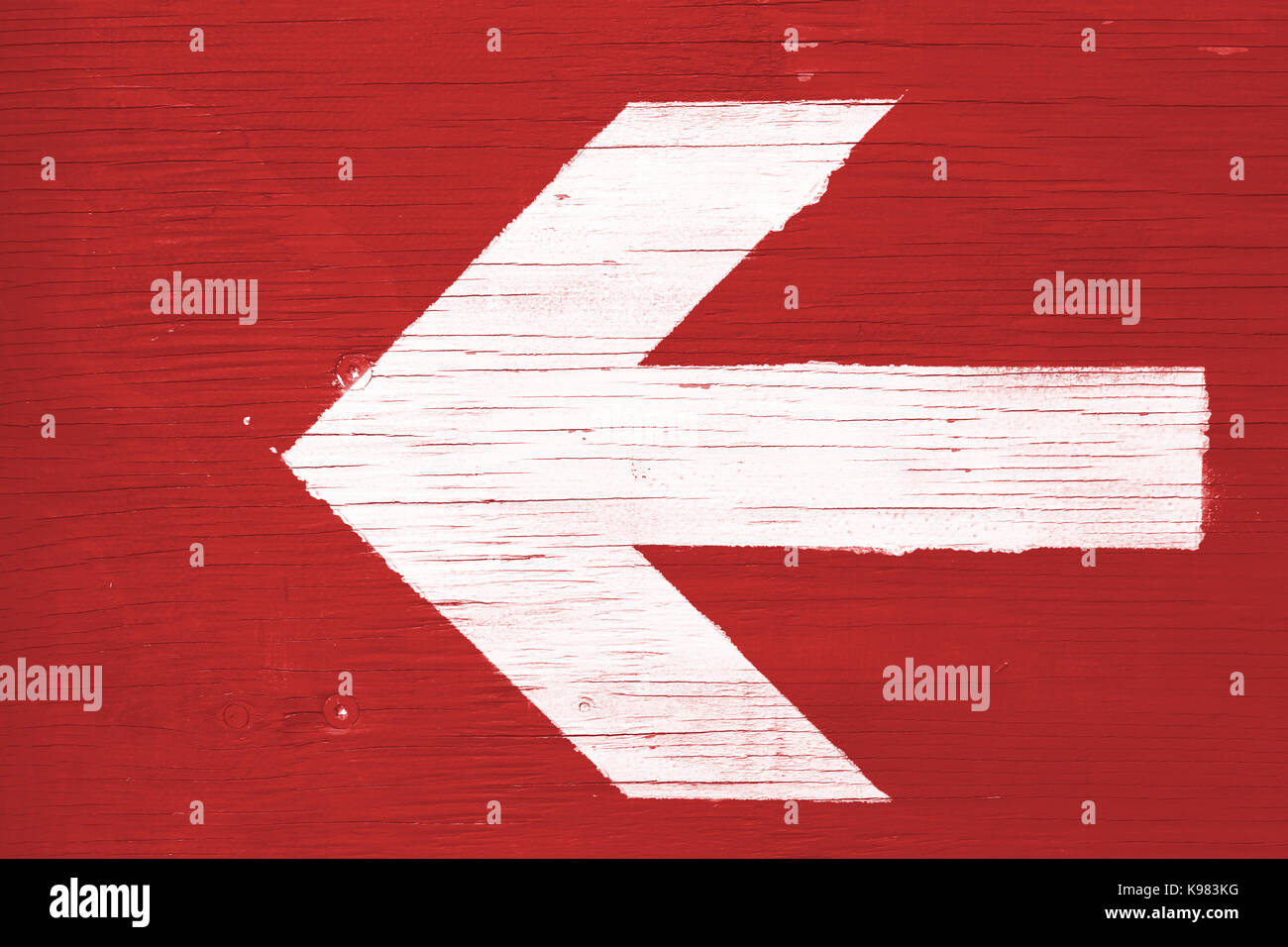 White directional arrow manually painted on a red wooden signboard ...