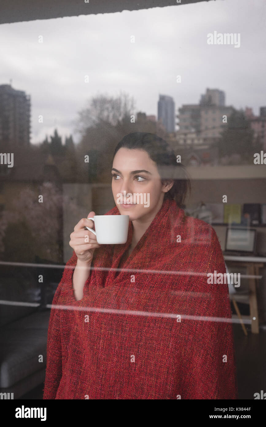 Contemplated young woman with coffee cup seen through glass window ...