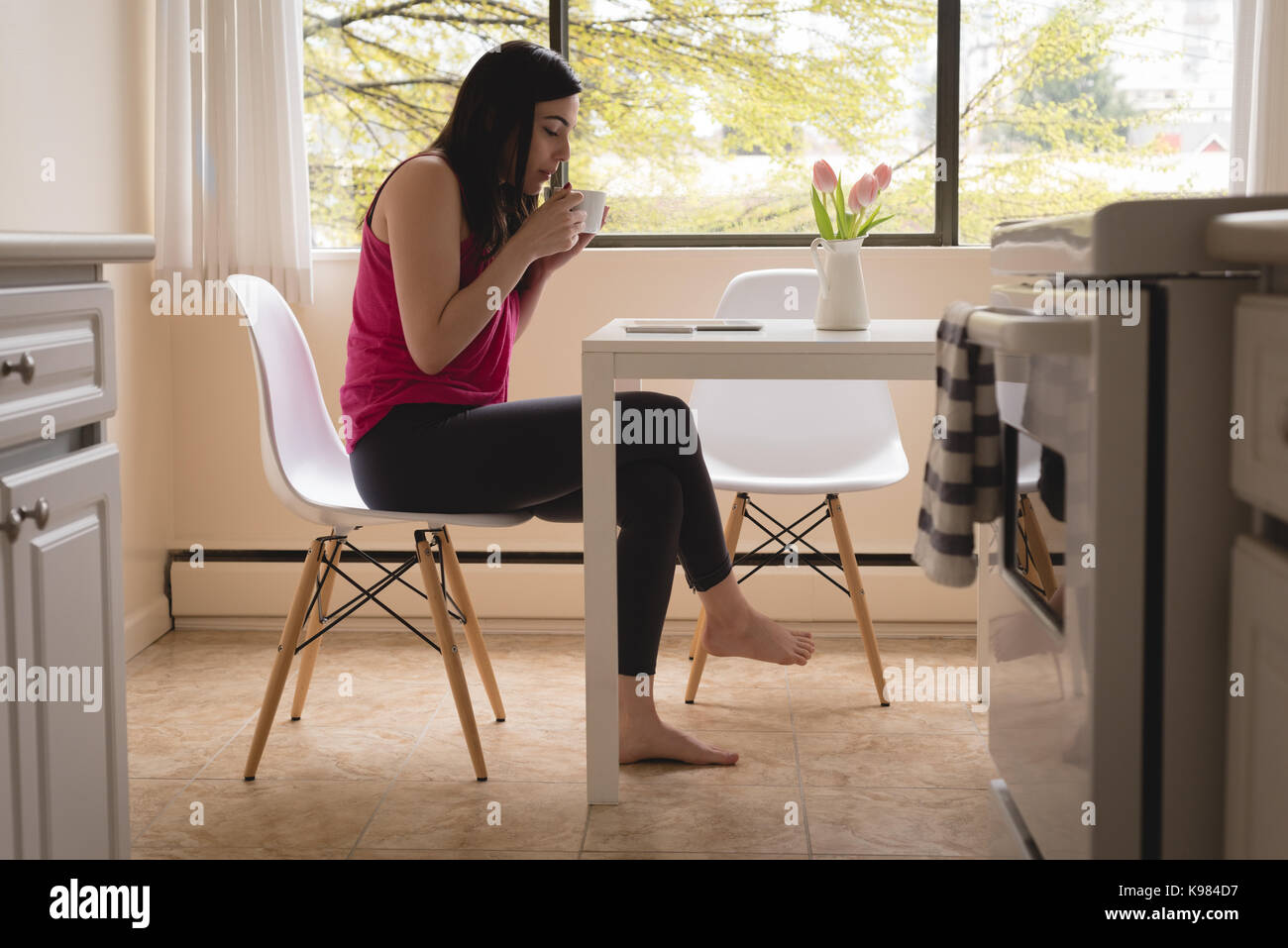 Side view of woman having coffee while sitting at table by window in ...