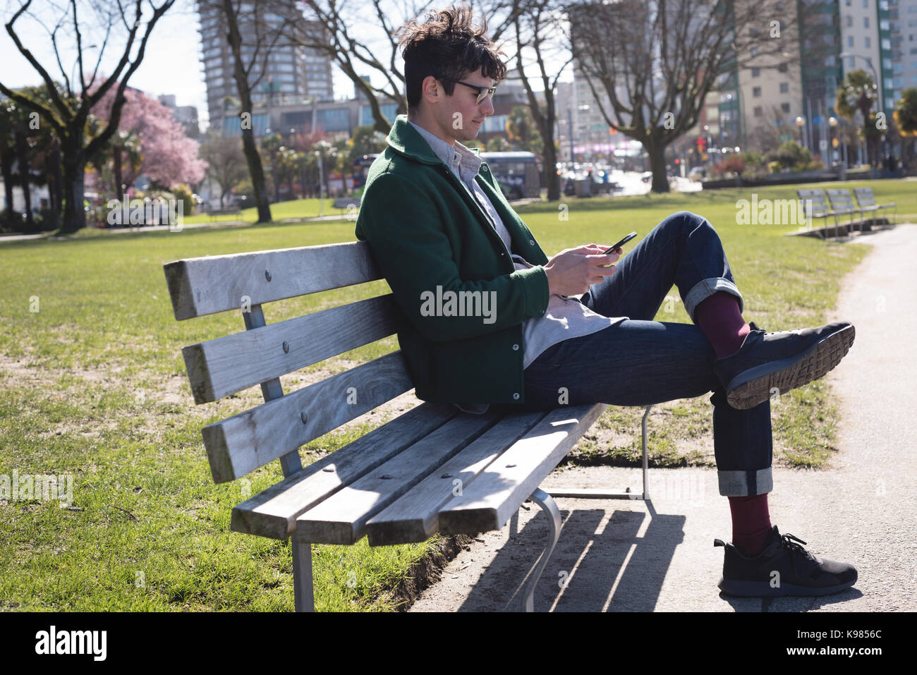 Man using mobile phone on bench at park Stock Photo - Alamy