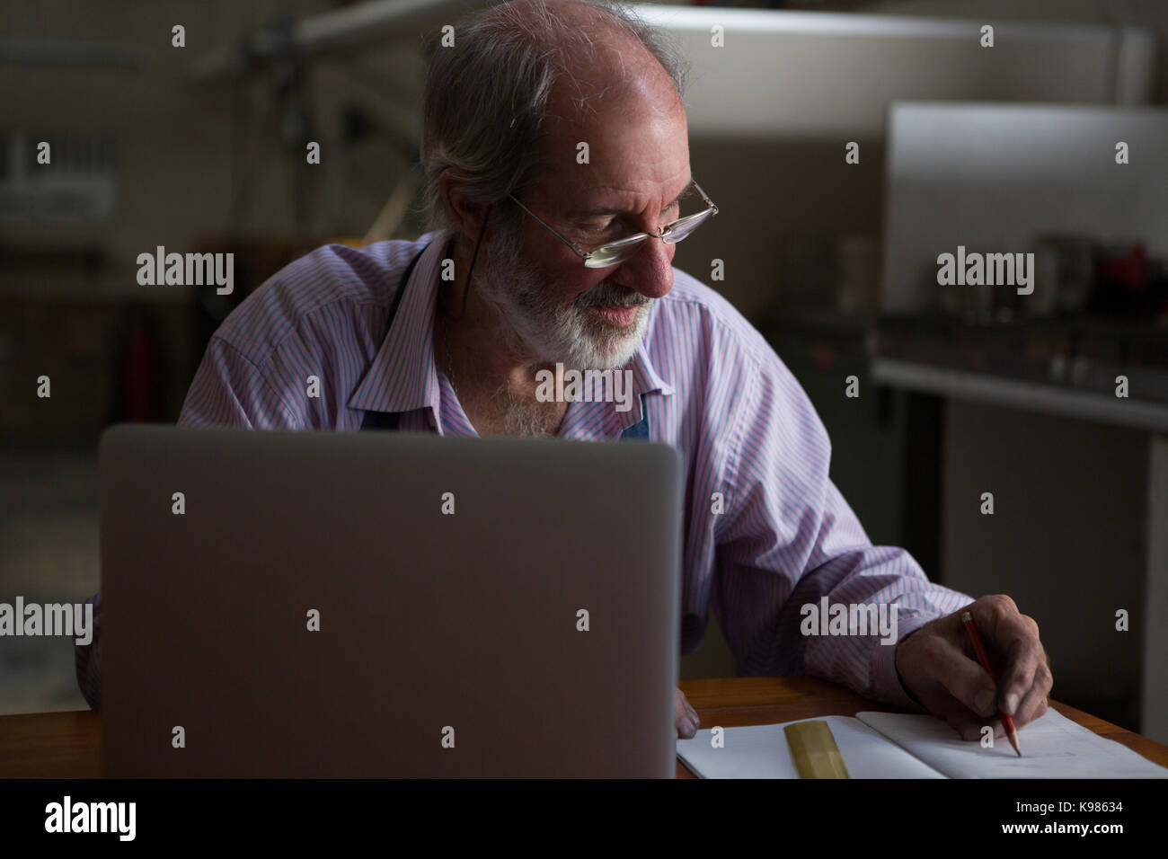 Goldsmith writing in book at desk in workshop Stock Photo - Alamy