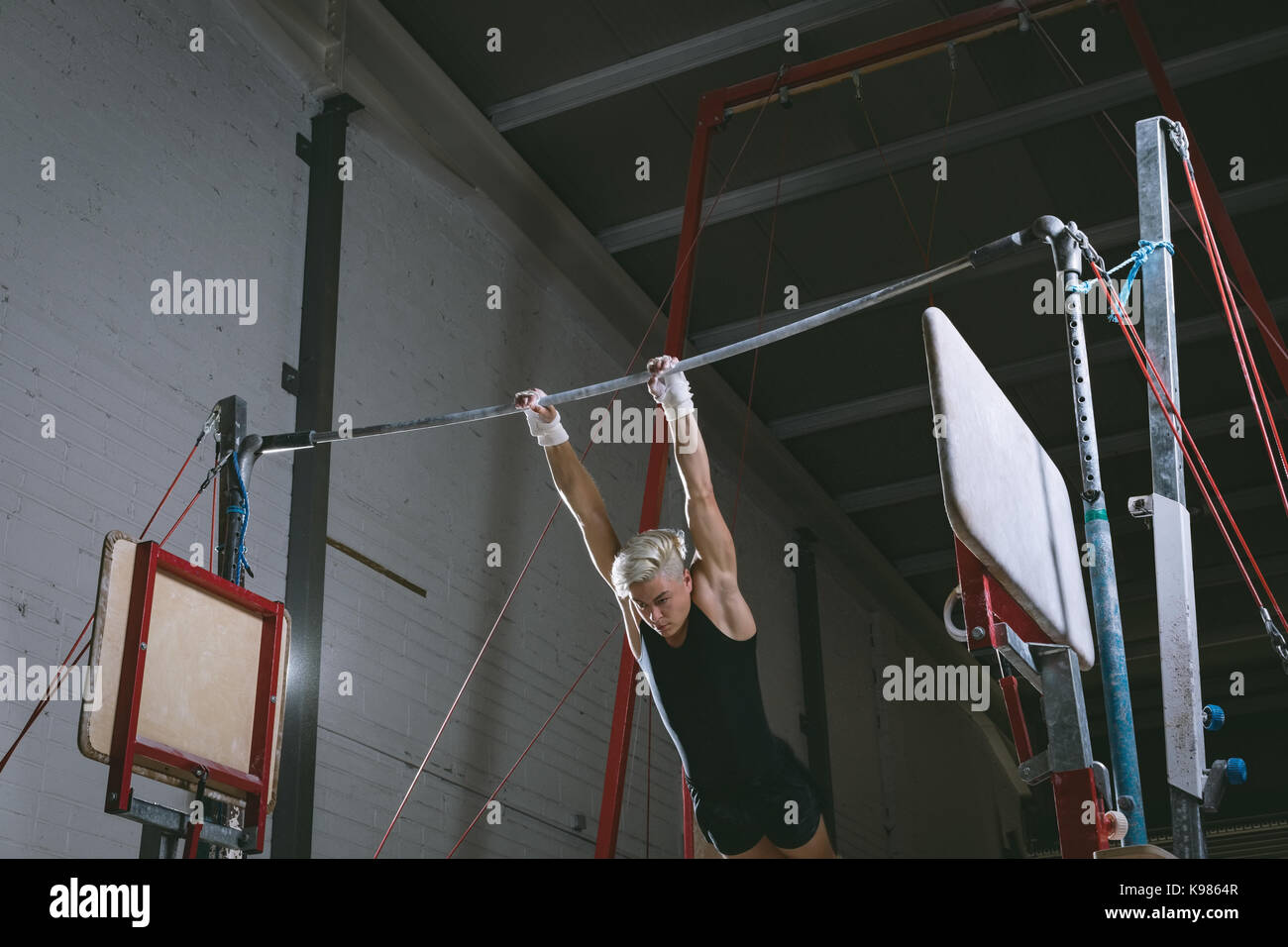 Male gymnast practicing gymnastics on the horizontal bar in the gym ...