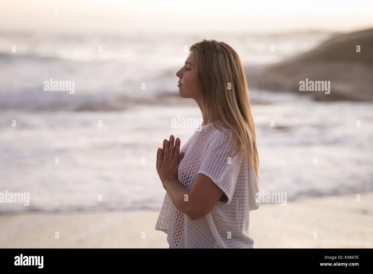 Side view of young woman meditating at beach during sunset Stock Photo ...