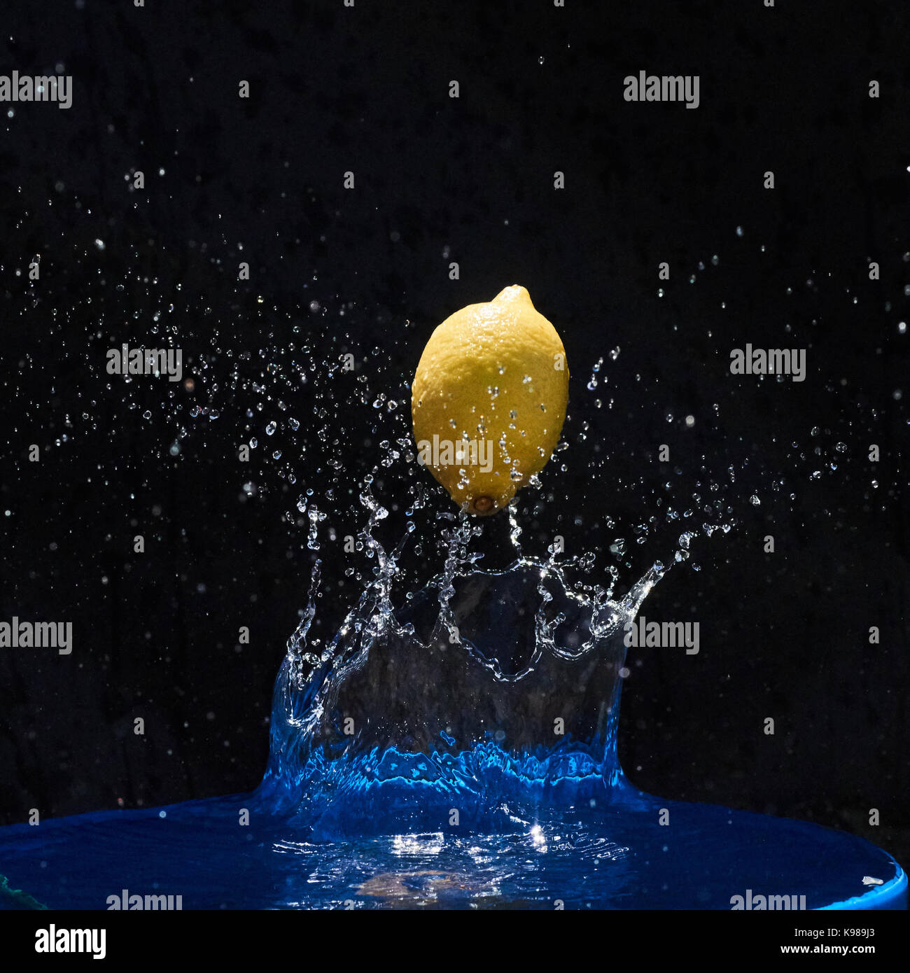 Juicy yellow lemon falls in water on a black background Stock Photo - Alamy