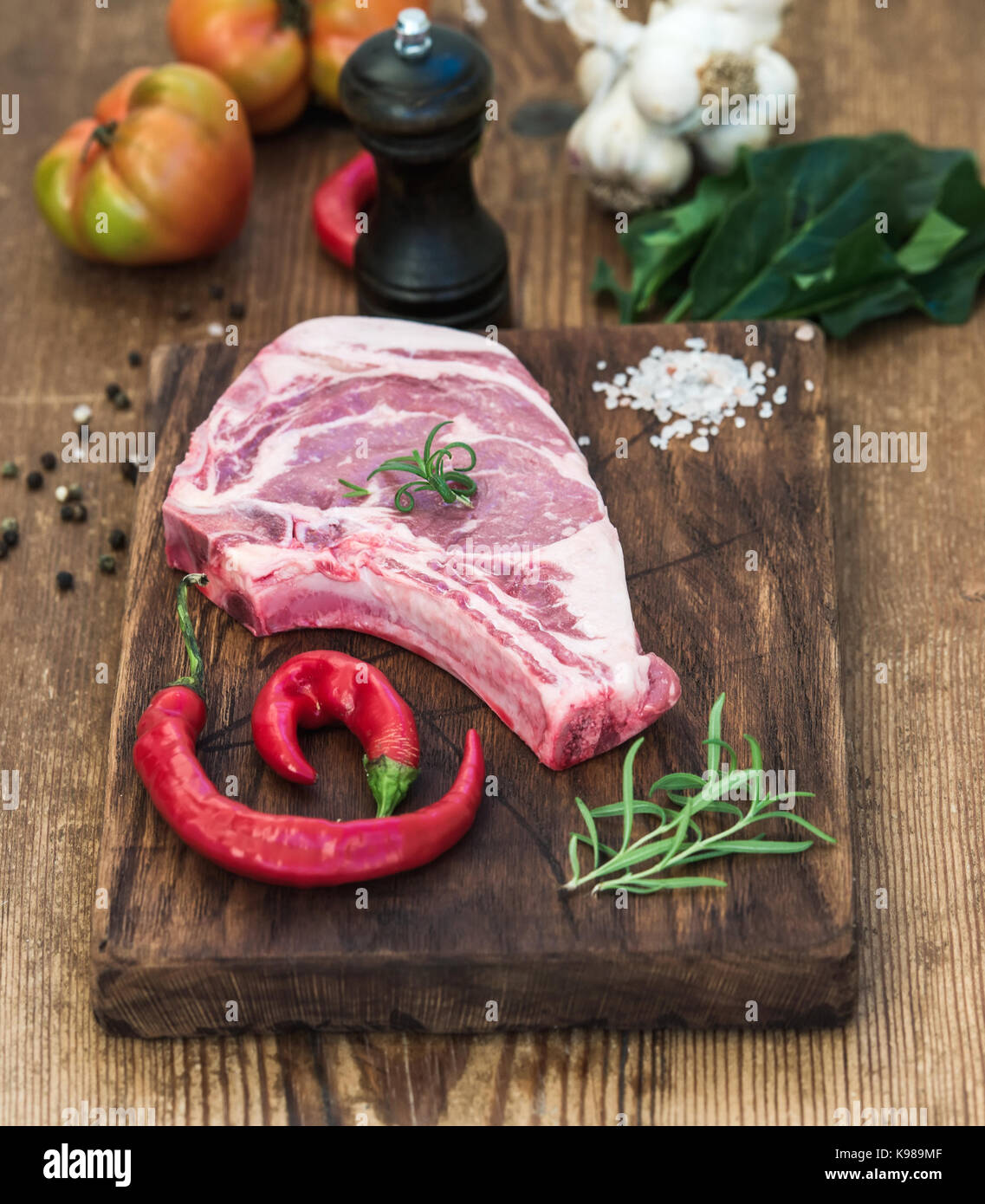 Raw fresh meat ribeye steak with salt, chili pepper, rosemary, tomatoes ...