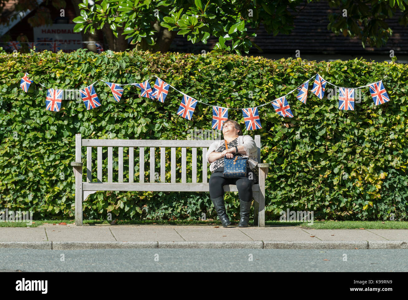A lady sat on a bench next to union jack flags with her eyes closed and ...