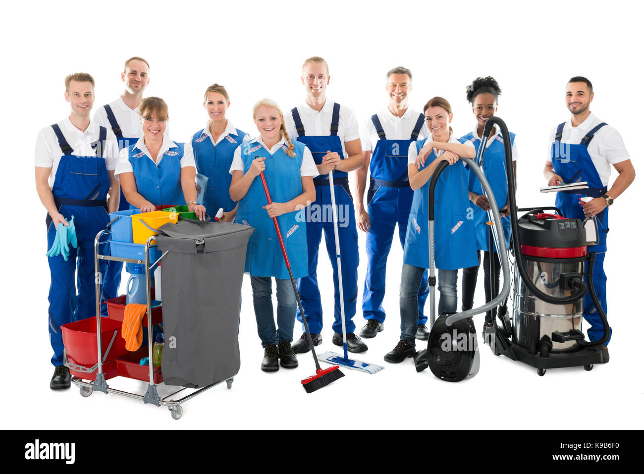 Portrait of happy janitors with cleaning equipment standing against ...