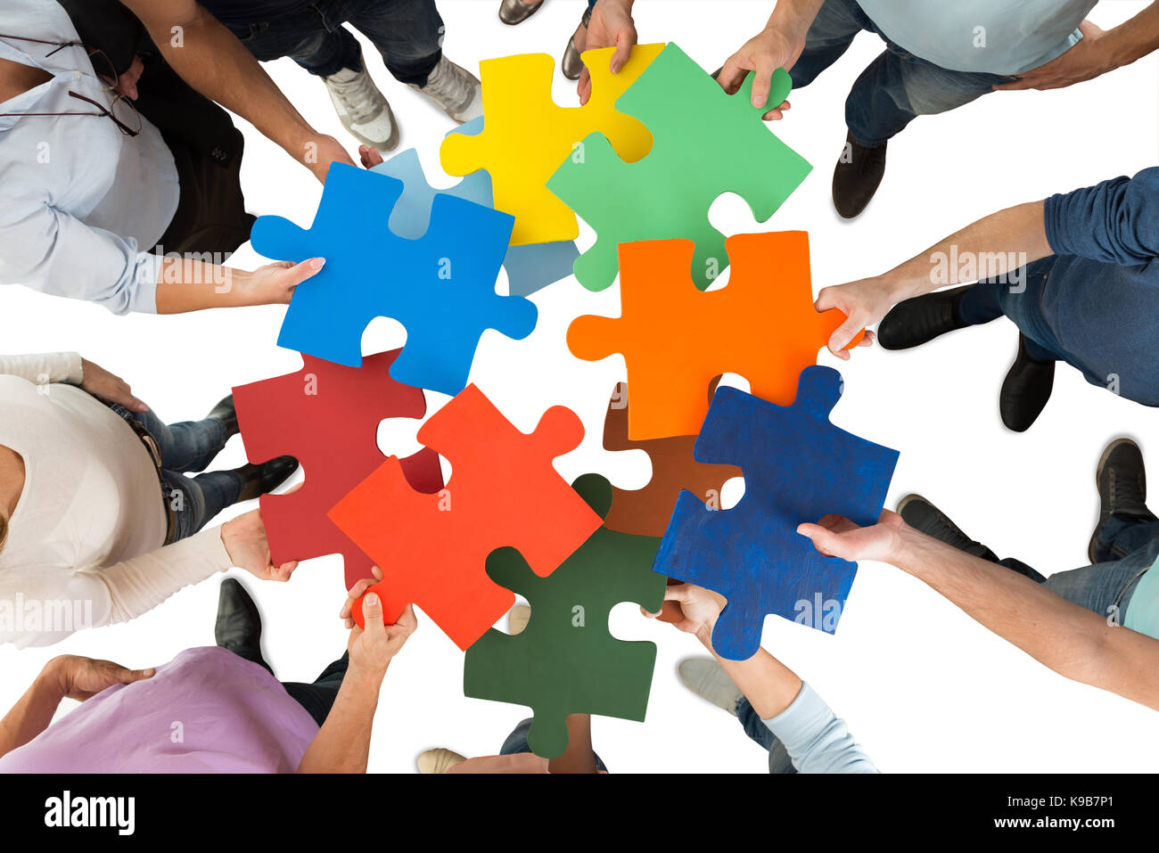 Directly above shot of people holding colorful puzzle pieces in huddle ...