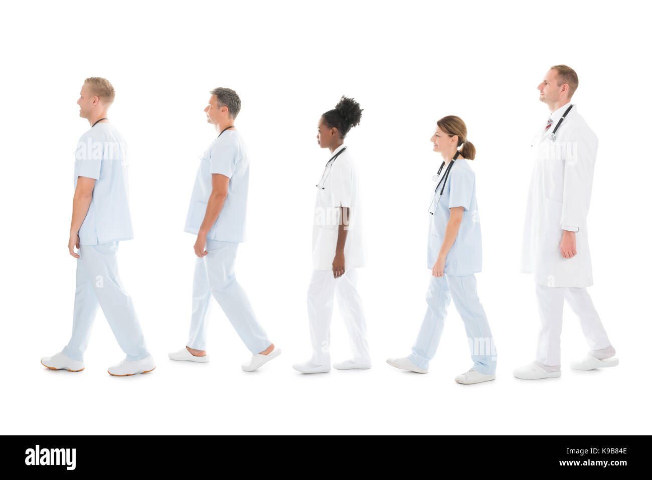 Full length side view of medical team walking in row against white ...
