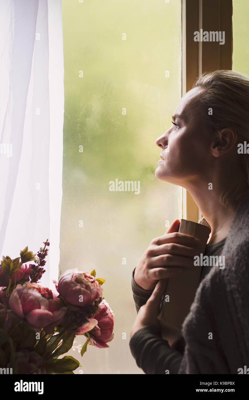 Woman looking longingly through window, daydreaming with favorite book ...