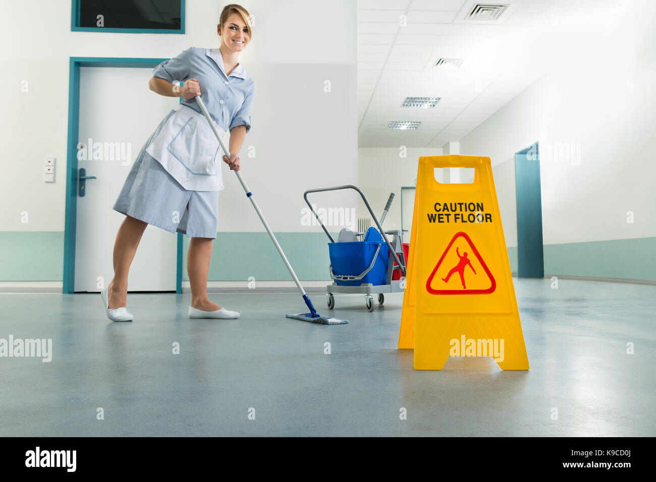 Happy Female Janitor With Mop And Wet Floor Sign On Floor Stock Photo ...