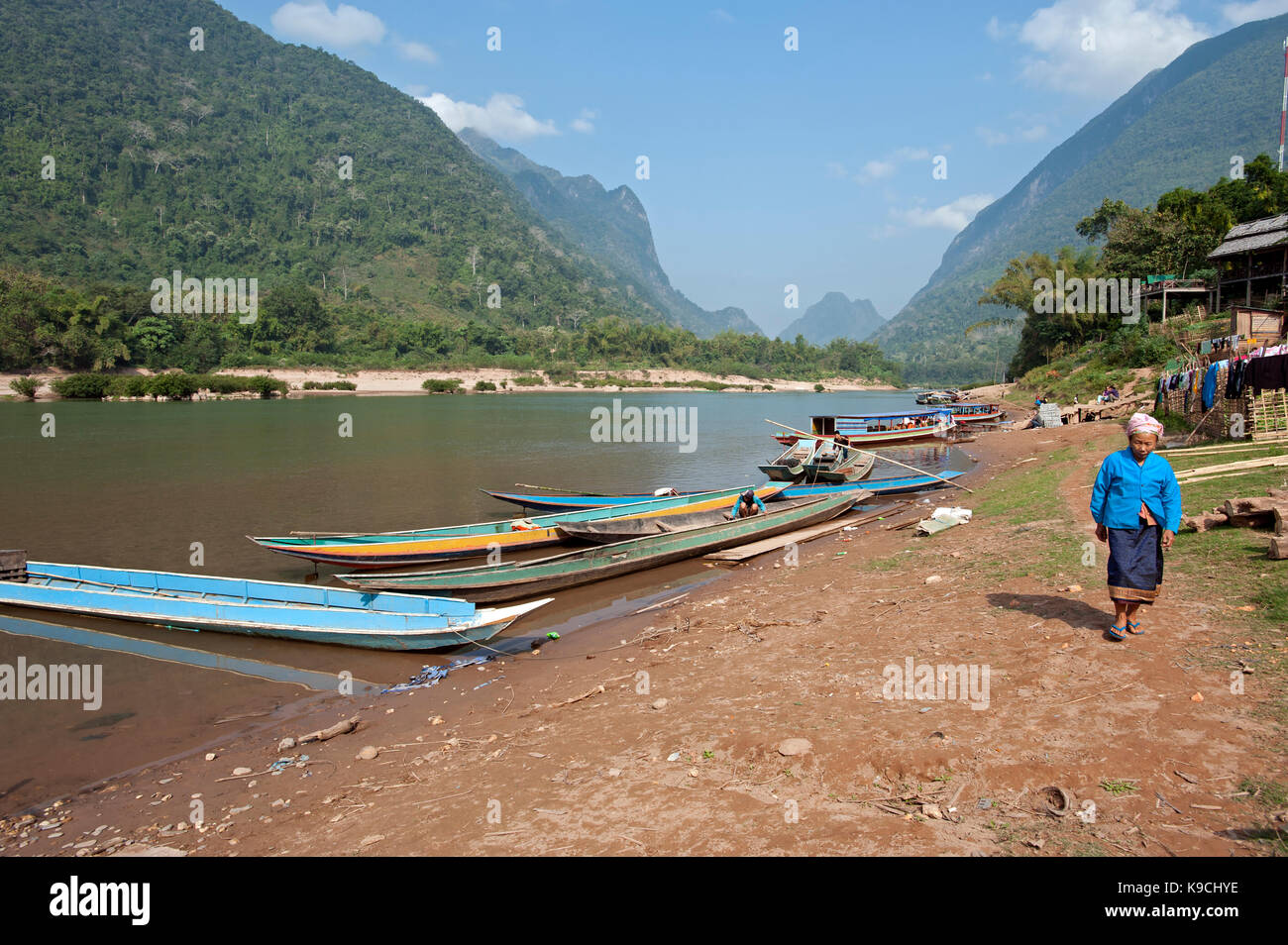 A Laotian woman wearing a sarong and turban walks along the riverbank ...