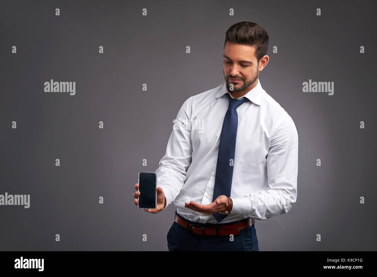 A confident handsome young man showing his phone to the camera and ...