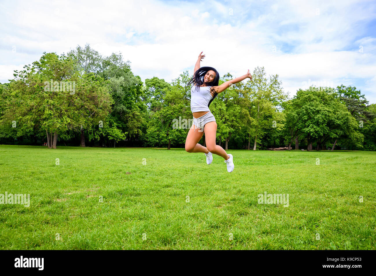 A beautiful young sporty girl jumping on a field in a park while ...