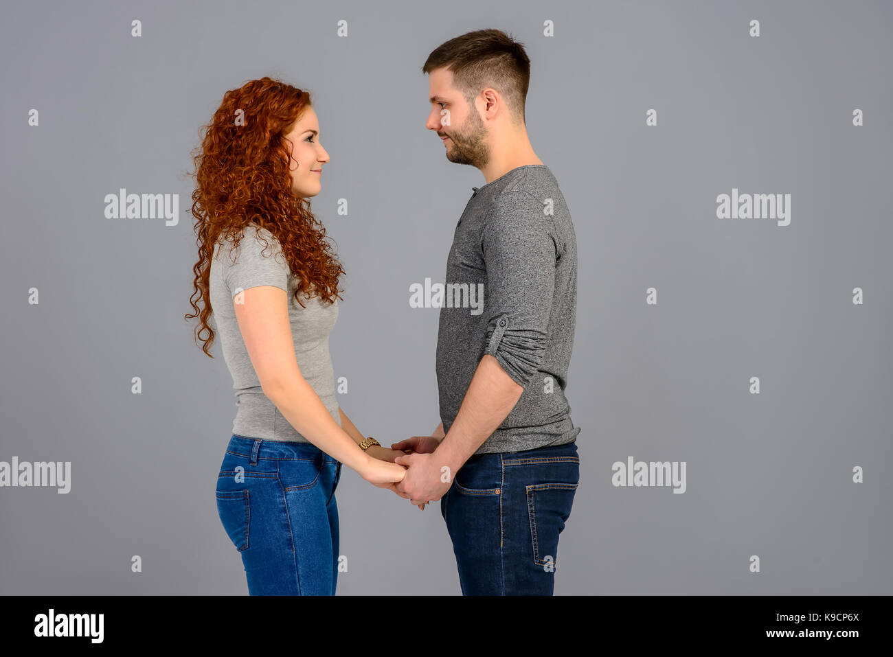 A beautiful young couple standing face to face and holding each others ...