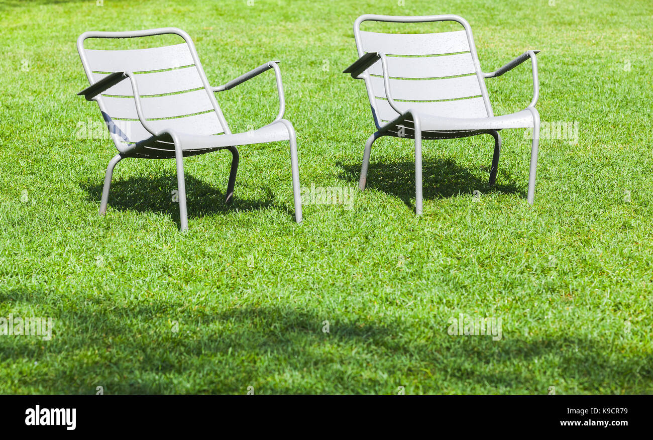 Two outdoor gray metal chairs stand on fresh green grass in summer park ...