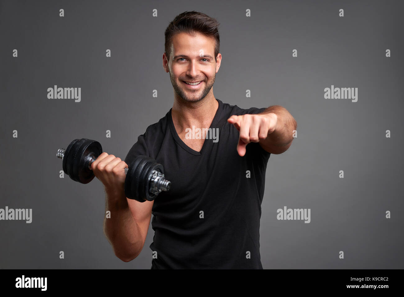 A handsome young man lifting weight smiling and pointing it to the ...