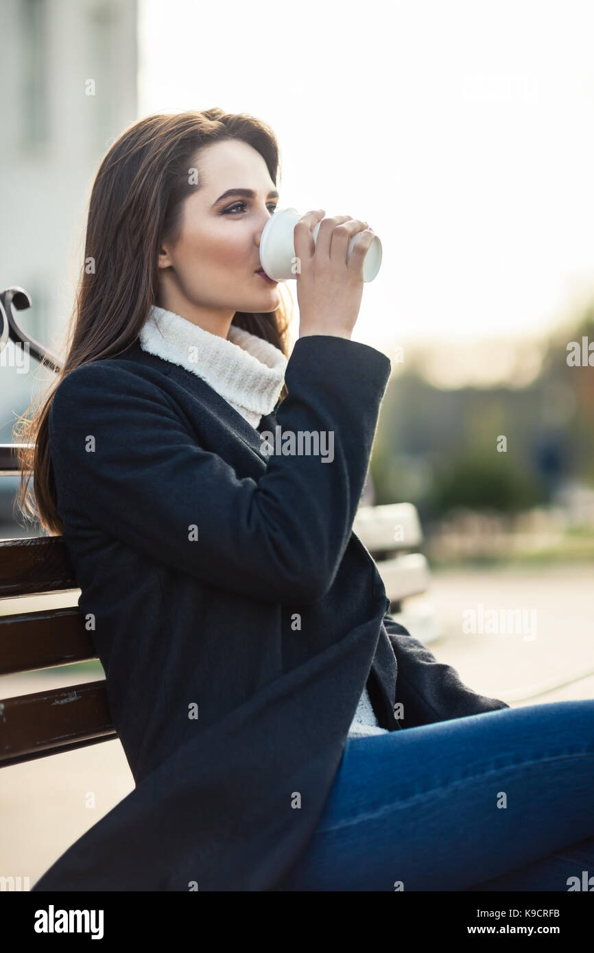 Beautiful woman drinking coffee sitting on a bench in city street ...
