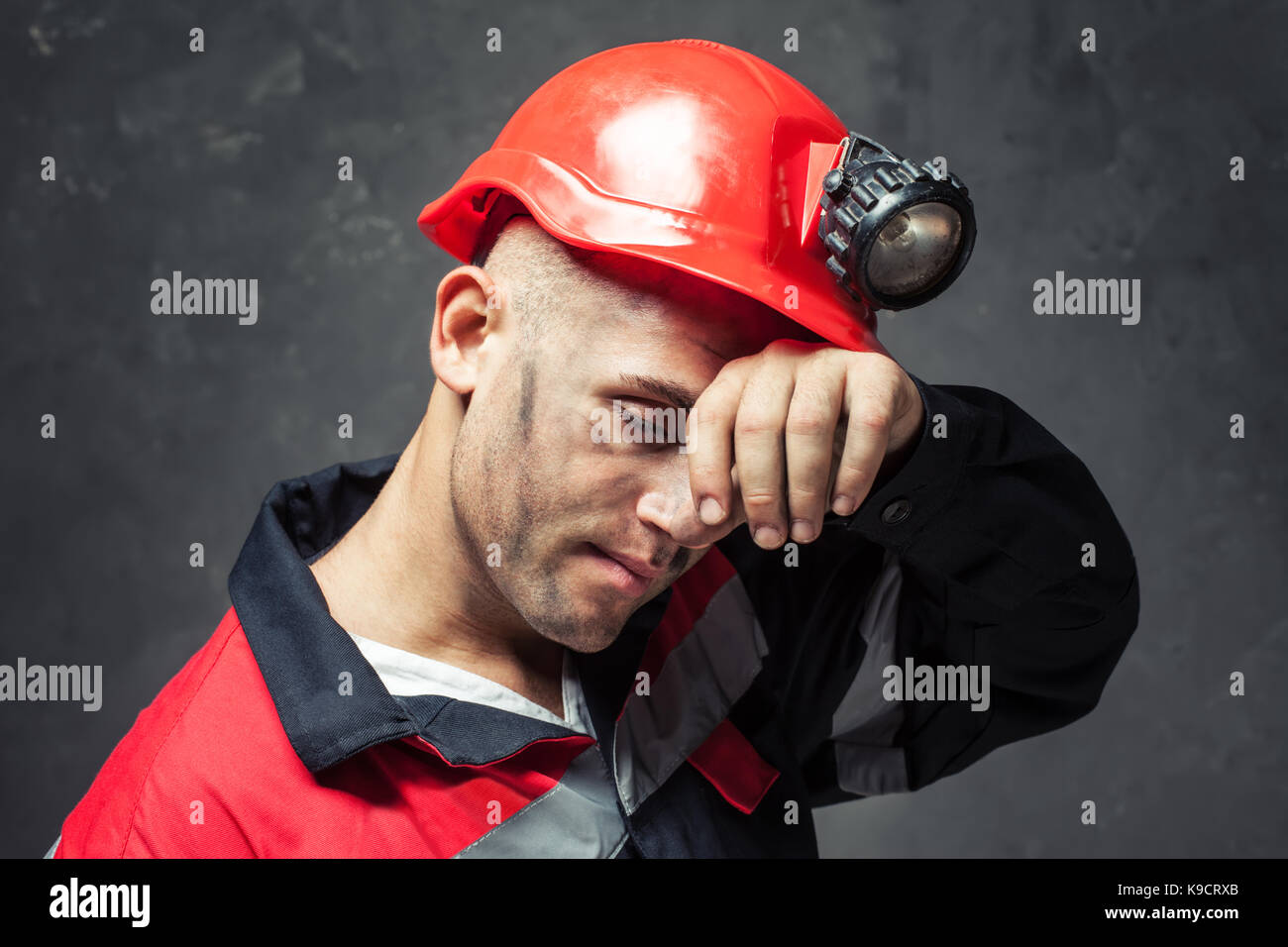 Portrait of tired coal miner wiping forehead his hand against a dark ...