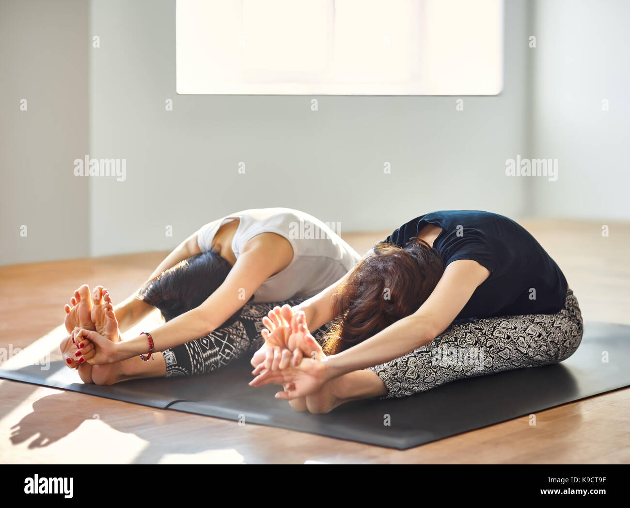 Two young women doing yoga asana seated forward bend. Paschimottanasana ...