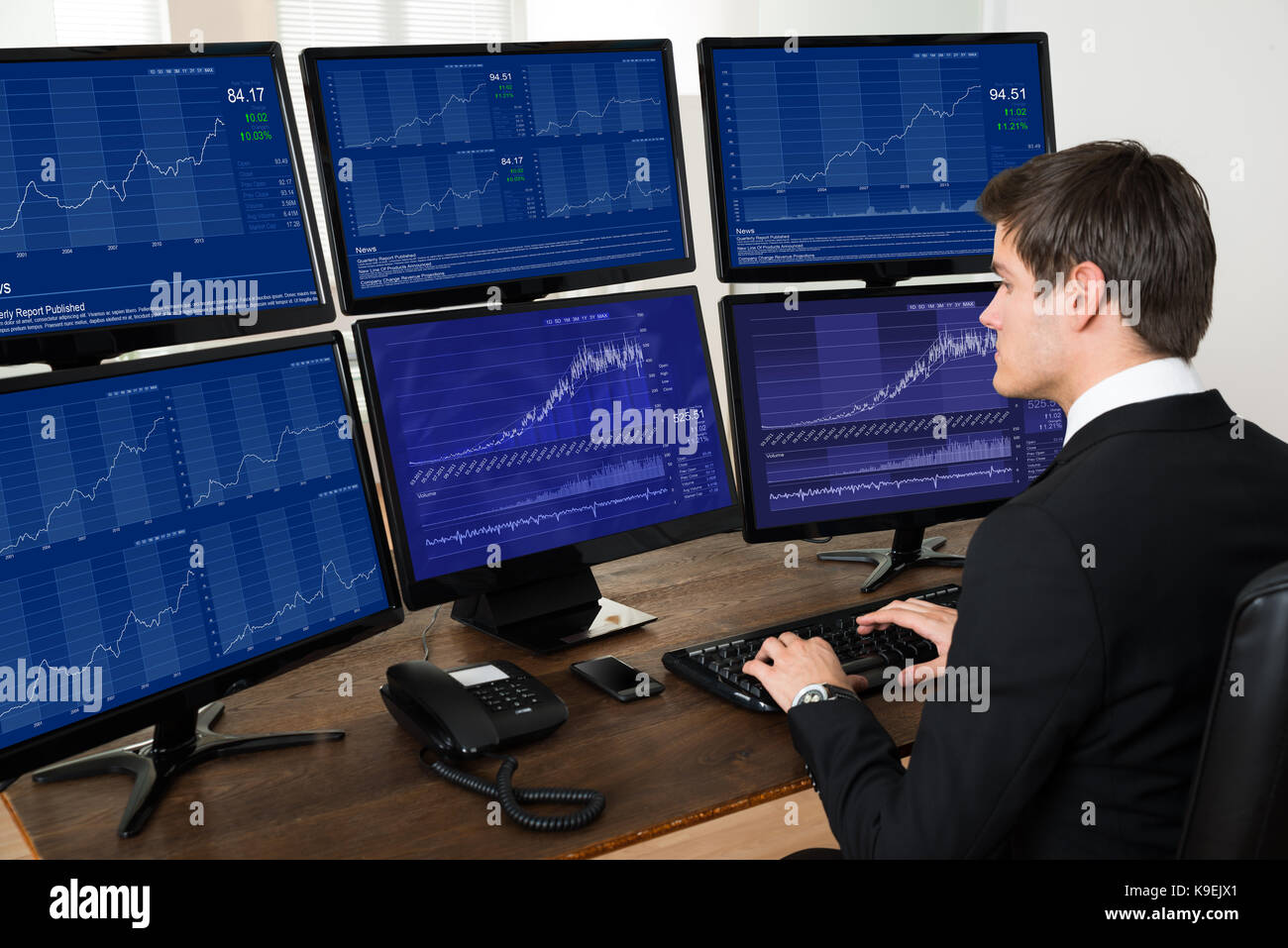 Young Businessman Working With Graphs On Six Computers At Desk Stock ...