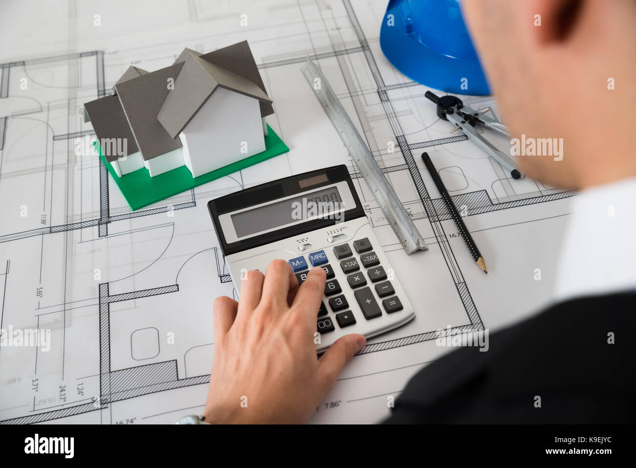 Close-up Of Architect With Blueprint Calculating On Calculator At Desk ...