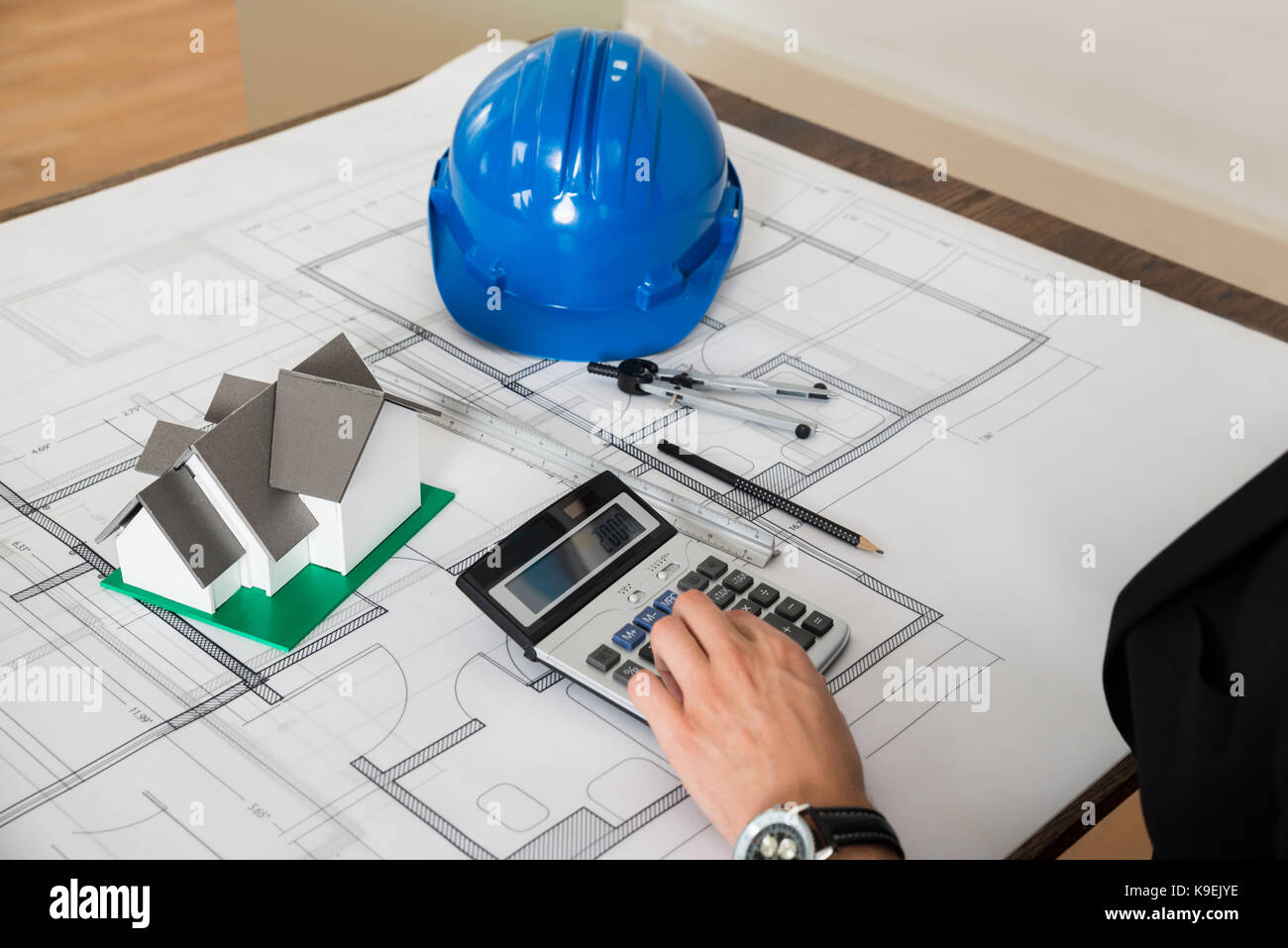 Close-up Of Architect With Blueprint Calculating On Calculator At Desk ...