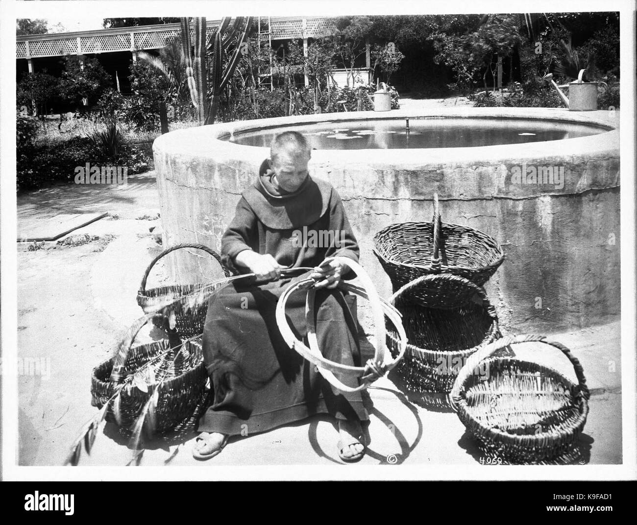 Monk sitting making baskets near the fountain in the garden at Mission ...