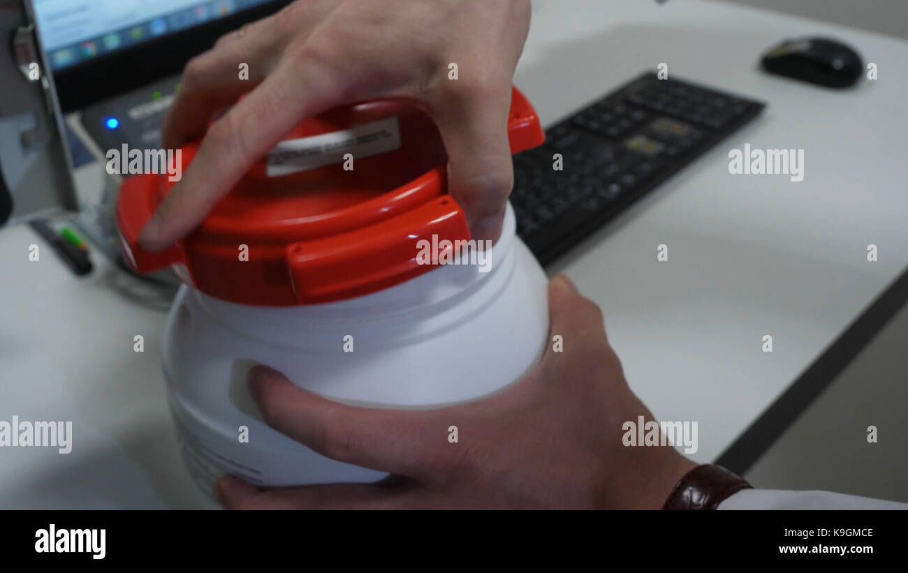 Chemical scientist opening white unlabeled plastic tank canister with ...