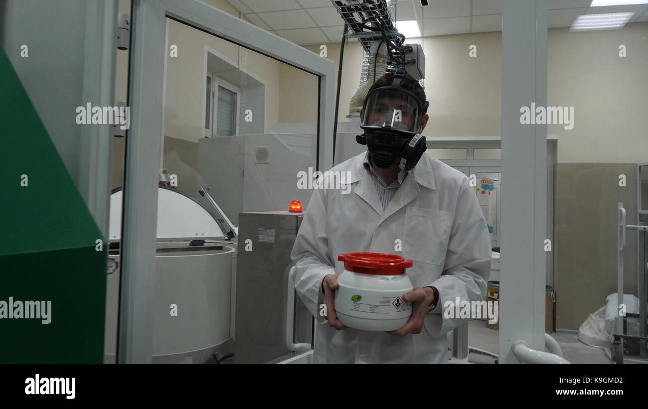 Scientist wearing protective suit and carrying a jar of toxic liquid ...