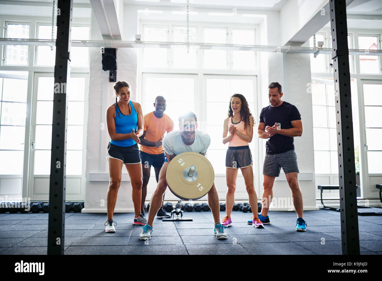 Smiling young man straining to lift weights in a gym with a diverse ...