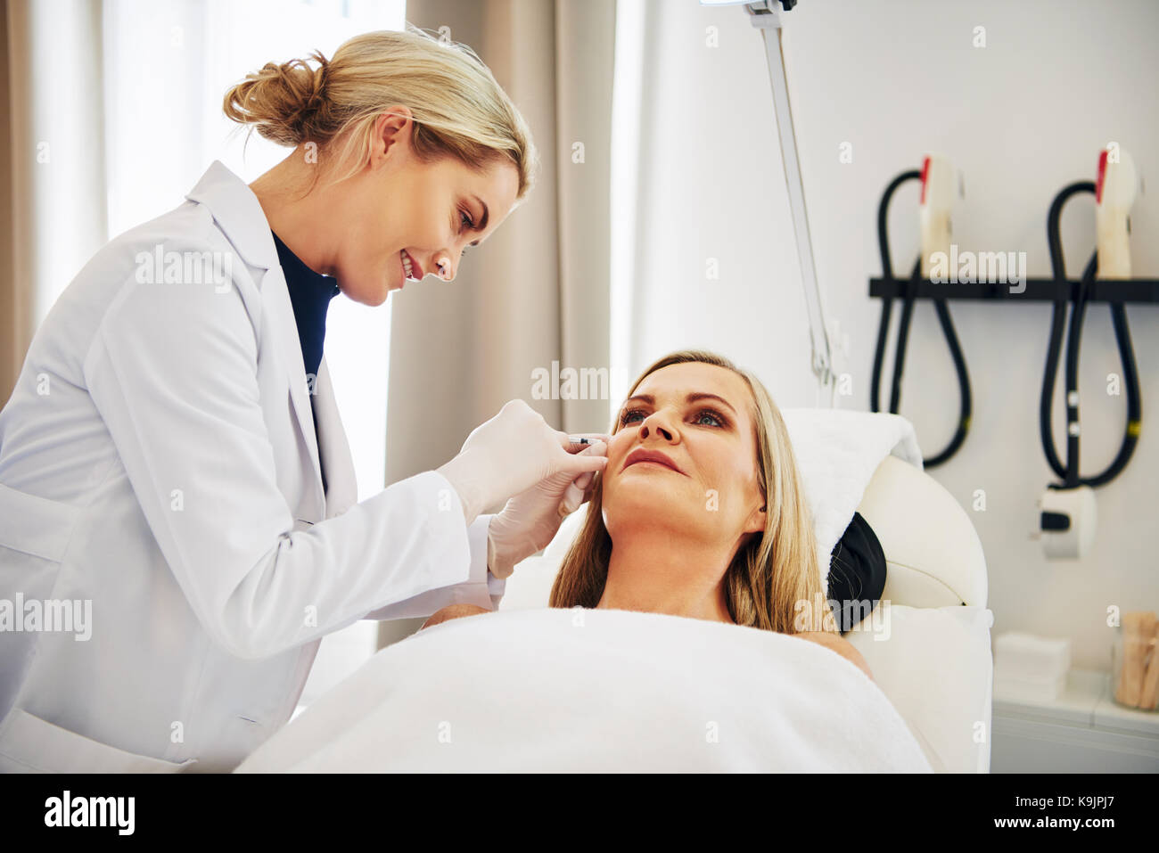Smiling young female doctor doing botox injections on the face of a ...